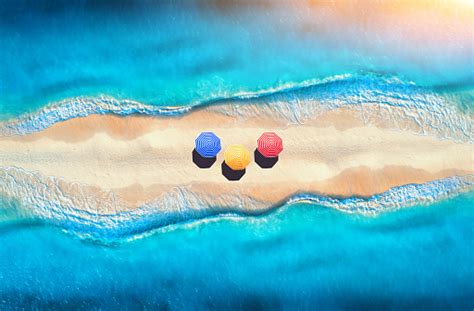 양쪽에 파도가 있는 투명한 푸른 바다와 석양에 화려한 우산이 있는 빈 모래 해변의 공중 전망 모래톱의 평면도 여름 여행 백사장이