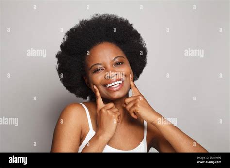 Attractive Woman Smiling And Touching Her Cheeks With Her Fingers Against Grey Studio Wall