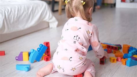 웃고 있는 어린 아이 화려한 큐브를 가지고 노는 금발의 미취학 아동 분홍색 잠옷을 입고 바닥에 앉아 집에 큰 창문이 있는 햇볕이 잘 드는 방 아이들의 초기 발달 2 3 살에