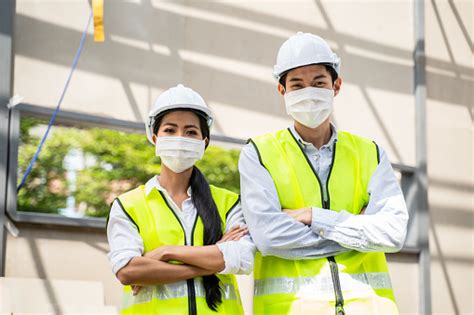 아시아 노동자들은 호조한 전염병 위기로 인해 건축 현장에서 보호얼굴 마스크를 쓰고 있다 Foreman 엔지니어는 자신있게 카메라를 바라보는 건설 측에서 일하는 건강을