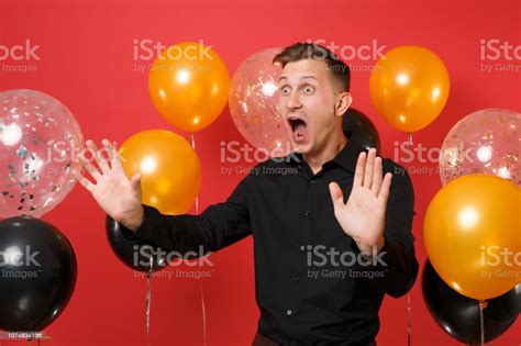 블랙 클래식 셔츠 빨간색 배경 공기 풍선에 지르고 손을 확산 축 하에 충격된 흥분된 젊은 남자 세인트 발렌타인의 여자 날 행복 한 새 해 생일 이랑 휴일 파티 개념 2019