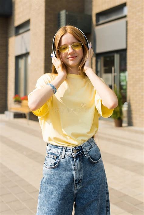 Happy Teenager Girl In A Yellow Shirt And Blue Jeans Is Wearing