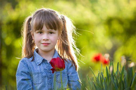 회색 눈과 밝은 빨간 튤립 꽃과 긴 머리와 귀여운 예쁜 미소 아이 소녀 흐린 햇볕이 잘 드는 녹색 보케 배경에 자연 개념에 사랑 감정에 대한 스톡 사진 및 기타 이미지
