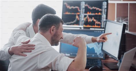 주식 중개인 팀이 디스플레이 화면이 있는 어두운 사무실에서 대화를 나누고 있습니다 투자 목적으로 데이터 그래프 및 보고서를