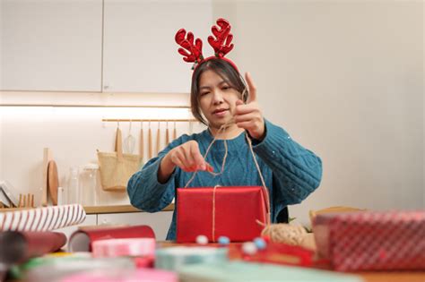 초록색 스웨터와 순록 뿔을 착용한 여성이 따뜻하고 장식된 공간에서 빨간 선물을 능숙하게 포장하고 있습니다 화려한 장식과 제작 용품이 그녀 주변에 흩어져 있습니다 40 44