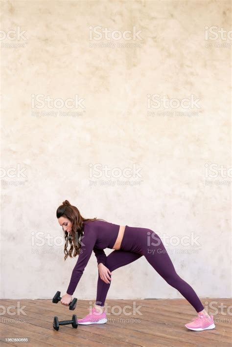 운동 하는 여자는 아령으로 훈련 팔과 다리의 근육을 펌핑 벽의 배경에 보라색 스포츠웨어를 입은 소녀의 사진 힘과 동기 부여 측면