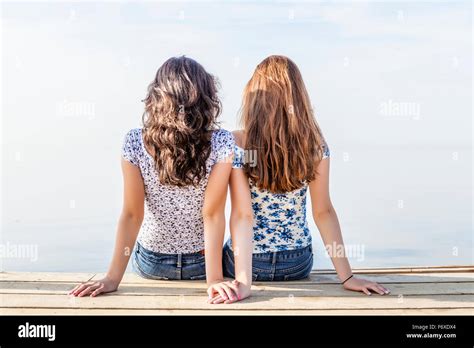 Two Girls Holding Hands Sitting Close Together At End Of A Dock Toronto Ontario Canada Stock