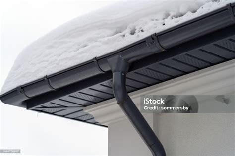 금속 다운 파이프 시스템 거터링 시스템 눈 아래 외부 하강 파이프 및 배수 파이프 회색 금속 타일로 만든 지붕과 겨울에 눈의 두꺼운 층으로 덮여 배수로와 집의 모서리