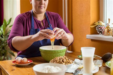 젊은 유럽 여 자가 나무 식탁 뒤에 부엌에 앉아 들고 손에 계란 그릇 이상에서 순간을 때 달걀 나누기 2 반 계란 따르고 그릇에 가정 생활에 대한 스톡 사진 및 기타 이미지