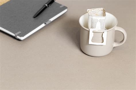 사무실 테이블에 큰 컵에 분쇄 커피와 드립 커피 가방 베이지 색 배경에 양조를위한 종이 가방 드립 커피 필터 패키지 복사 공간이있는 사이드 뷰 가방에 대한 스톡 사진 및