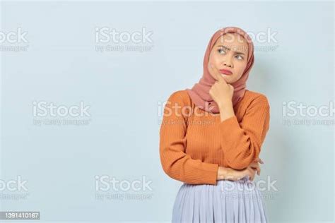 갈색 스웨터를 입은 아름다운 젊은 아시아 무슬림 여성의 초상화는 질문에 대해 진지하게 생각하고 흰색 배경에 고립 된 복사 공간을 바라 봅니다 무슬림 생활 방식 개념 25