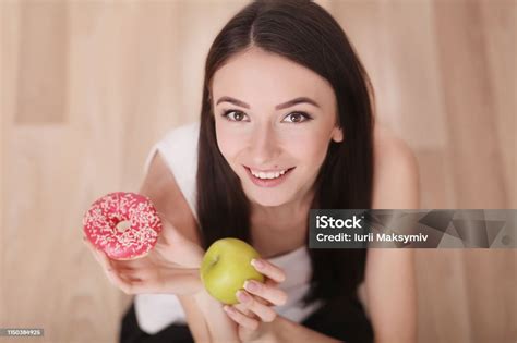 다이어트 무게 저울에 체중을 측정 하는 여성은 도넛과 사과를 들고 있습니다 과자는 건강에 해로운 정크 푸드입니다 다이어트 건강