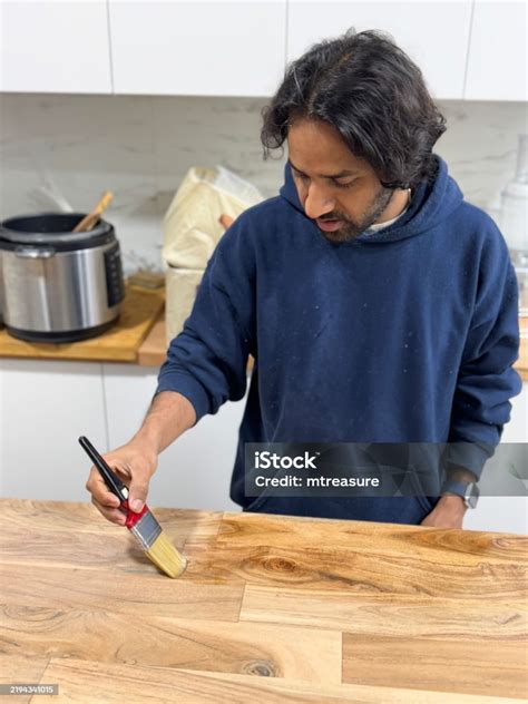 붓을 사용하여 부엌 나무 조리대에 기름을 바르는 인도 남자 페인트 칠하는 카운터 나무를 밀봉하고 보존하는 이미지 전경에 초점을 맞춥니다 30 34세에 대한 스톡 사진 및