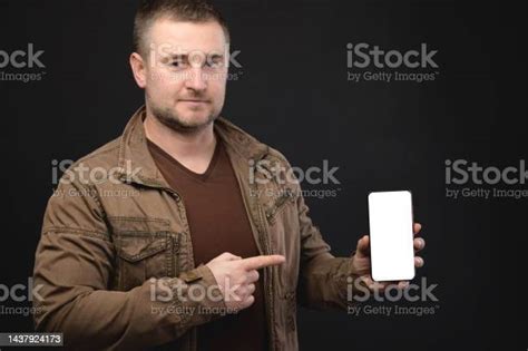 캐주얼 한 옷을 입은 성숙한 중년 남성이 스마트 폰에 응용 프로그램을 제시하면서 손에 들고 컷 아웃 모형 화면을 보여줍니다 스튜디오 초상화 긍정적인 감정 표현에 대한 스톡