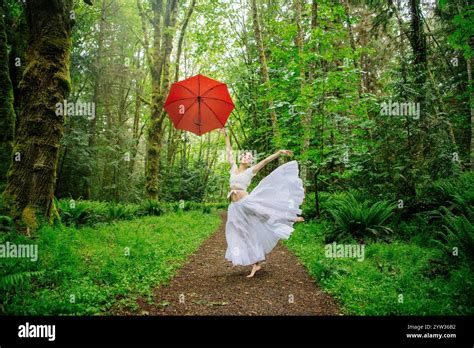 A Joyful Ballet Dancer Holding A Red Umbrella Twirls Along A Forest