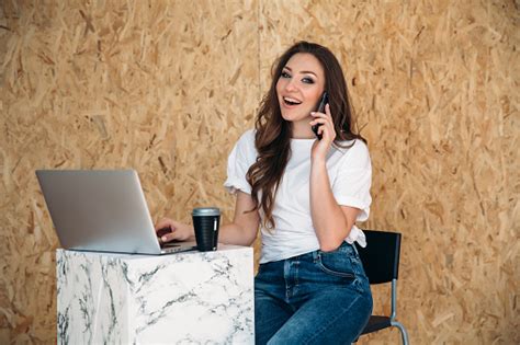 아름 다운 세련 된 젊은 유럽 현대 기술에 가벼운 평상복 작품에서 옷을 입고 이자와 함께 전화를 통해 대화를 실시 그녀의 맛 있는 향기로운 커피 음료 갈색 바탕에 고립 된