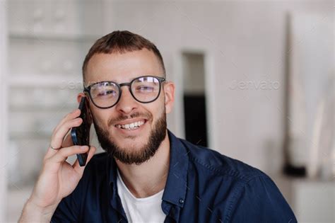 Young Beardy American Man Talks By Phone Looks Aside Smiles Cheerful Caucasian Guy In Glasses