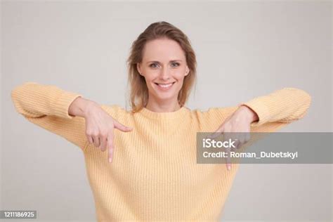 금발 의 여자 초상화 로 가리키는 미소 친절 하 고 카메라를 응시 시도 제품 Ot 회색 배경 위에 복사 공간을 봐 노란색 스웨터를 입고 얼굴 표현 곱슬 머리에 대한 스톡