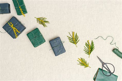 녹색 파란색 공예 종이의 선물 상자는 베이지 색 테이블에 천연 미모사 꽃을 장식했습니다 봄 휴가 선물 포장 자연 장식 선물 플랫