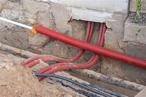 빨간색 골판지 파이프의 전기 케이블은 거리의 지하에 묻혀 있습니다 전기 케이블 인프라 설치의 허브 많은 에너지를 가진 건설 현장 케이블과 수도관 0명에 대한 스톡 사진 및