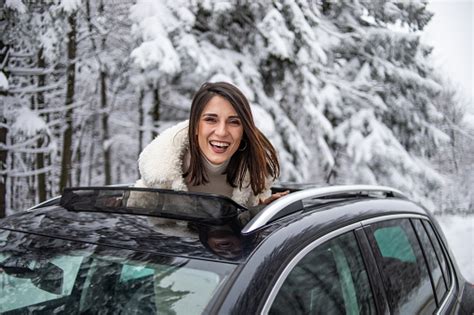 아름다운 젊은 여성이 눈 덮인 숲을 통과하는 길에 쉬고 차의 선루프를 통해 서있는 아름다운 자연을 관찰합니다 겨울 방학 30 34세에 대한 스톡 사진 및 기타 이미지
