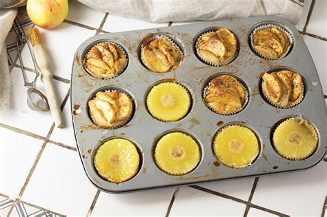 파인애플 서클과 사과 슬라이스를 컵케이크 머핀 트레이에 넣은 머핀 컵케이크는 페이스트리 브러쉬로 근처 의 부엌 흰색 타일에 놓습니다 요리 책 조리법 상단보기를위한 케이크