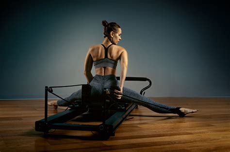 개혁가 침대와 필라테스 운동을하고 어린 소녀 개혁가 회색 배경 낮은 키 예술 조명에 아름 다운 슬림 피트 니스 트레이너 피트니스 컨셉 가냘픈에 대한 스톡 사진 및 기타