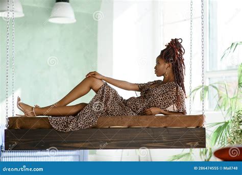 Black Fashion Model Lying On The Swing With Chains In The Light Room