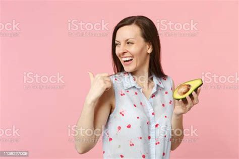 여름 옷을 옆에 젊은 여자를 웃 고 밖으로 분홍색 파스텔 배경에 고립 된 신선한 잘 익은 아보카도 과일의 절반을 잡아 사람들은 생생한 라이프 스타일 휴식 휴가 개념입니다