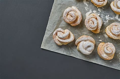 종이에 가루 설탕을 넣은 장미 형태의 많은 수제 구운 빵은 어두운 콘크리트 책상 위에 놓여 있습니다 제과 작업장 텍스트의