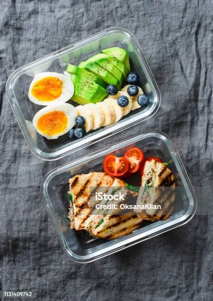 달 콤 하 고 짭짤한 음식으로 구성 된 2 개의 건강 한 오피스 런치 박스 삶은 달걀 아보카도 참치 시금치 치즈 샌드위치와 회색 배경에 과일 평면도 갈색 빵에 대한 스톡