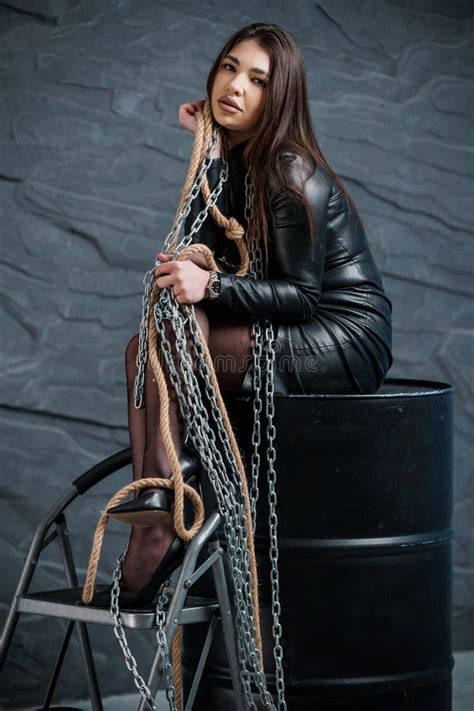 A Striking Young Woman With Long Dark Hair Sits On A Black Barrel