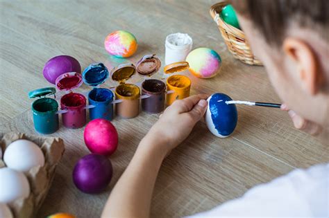 흰색 티셔츠를 입은 소녀는 페인트와 브러시 클로즈업으로 부활절 색 달걀을 칠합니다 부활절 봄 페인트 달걀 아이는 페인트 칠한