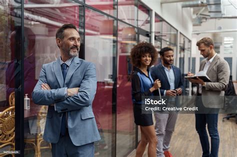 사무실에 서서 동료들의 배경에 옆을 바라 보는 잘 생긴 사업가 미소 짓기 20 24세에 대한 스톡 사진 및 기타 이미지 20 24세 25 29세 30 34세 Istock