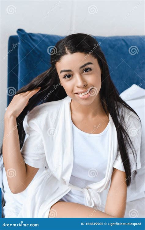 Smiling Beautiful Mixed Race Girl In White Robe Sitting On Bed And