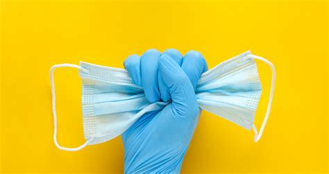 노란 배경에 일회용 의료 용 얼굴 마스크를 잡는 장갑 손 의료 종사자 개념에 대한 개인 보호 장비 Ppe의 부족에 분노