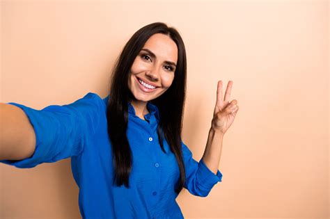 기쁜 사랑스러운 긍정적 인 아가씨의 사진은 세련된 옷을 입고 베이지 색 배경에 격리 된 빈 공간 데몬 스타테 Vsign 빈 공간을 착용합니다 갈색 머리에 대한 스톡 사진 및