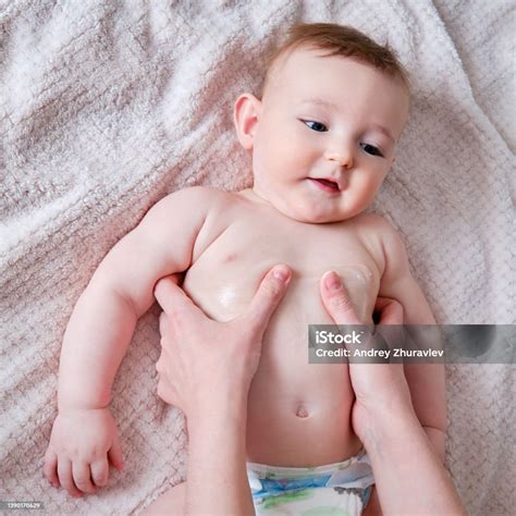 어머니의 손은 행복한 유아 아기에게 크림을 묻히고 있습니다 엄마가 여섯 달에서 일곱 달 된 소파에서 웃는 유아 아이를 마사지합니다 보습제에 대한 스톡 사진 및 기타 이미지