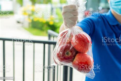 파란 유니폼을 입은 푸드 택배 서비스 맨 집 집에서 고객을 기다리는 신선한 빨간 사과 과일을 들고 있는 보호 얼굴 마스크 익스프레스 배달 바이러스 발생 테이크아웃 음식 배달