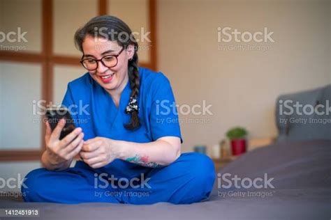 스마트 폰을 사용하여 침대에 앉아있는 스크럽이있는 여성 수술복에 대한 스톡 사진 및 기타 이미지 수술복 여성 행복 Istock