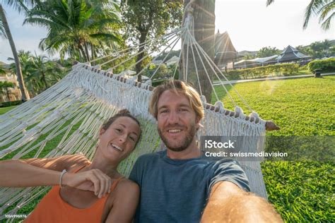열 대 기후사람들이 여행 모바일 장치 기술에서 멋진 순간을 포착 하는 자연과 인생을 즐기는 휴가에 편안한 흰색 해먹에 젊은 부부 복용 Selfie 2명에 대한 스톡 사진 및