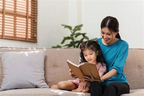 Mother And Daughter Reading A Book Together On A Cozy Sofa In A Bright