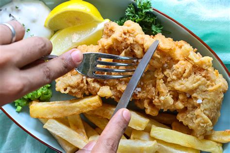 금속 나이프와 포크를 사용하여 소금으로 맛을 낸 피쉬 앤 칩스를 먹는 알아볼 수 없는 사람의 전체 프레임 이미지 타원형 오리