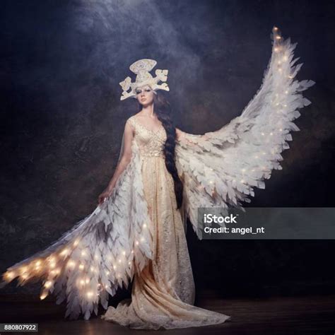 예술 여자 고급 스러운 긴 드레스와 멋진 투구에 날개를 가진 천사 어두운 배경에 포즈 빛나는 날개를 가진 소녀 새 갈색 머리에