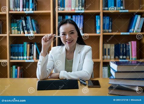 Southeast Asian Female Lecturer Sits At A Small Table Working At The