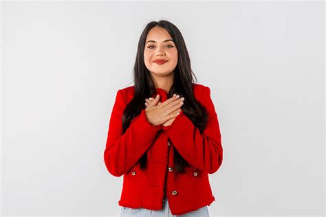 걱정하다 미소 짓는 아름다운 젊은 여자는 가슴에 손을 얹고 카메라를 부드럽게 바라보며 하얀 배경 위에 서 있다 정직한 미소를 가진 행복하고 멋진 매력적인 갈색 머리 여성의