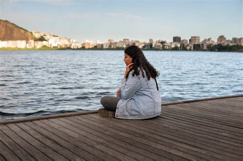 Грустная и созерцательная женщина сидит у озера Бесплатно Фото