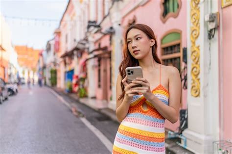 Z세대 아시아 여성은 스마트폰을 사용하여 여행 중 푸켓 올드타운의 매력을 탐험하고 언제 어디서나 소셜 미디어에 연결합니다 장치를 사용하는 젊은 여성입니다 장치와의 연결