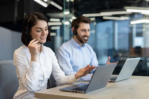 현대적인 개방형 사무실 환경에서 헤드셋이 장착된 노트북을 사용하여 비디오 회의 중 미소 짓는 사무실 직원 2명에 대한 스톡 사진 및 기타 이미지 Istock