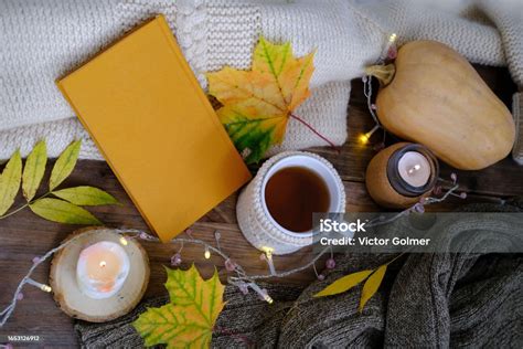 찻잔 모직 옷 노란 나뭇잎 나무 테이블에 있는 책 화환 촛불이 타오르고 있고 티 파티의 개념 좋은 날씨 아늑한 가을을 껴안고